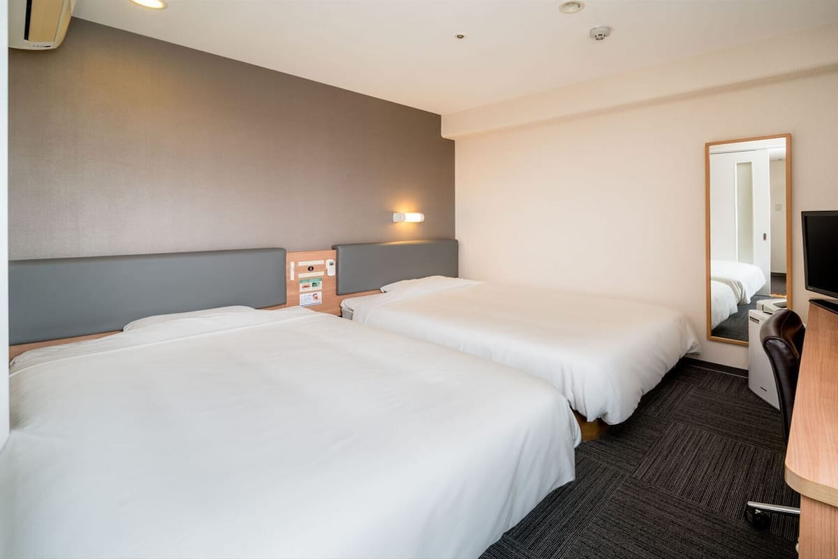 Quarto de hotel com duas camas, uma mesa de trabalho com televisão, um espelho e telefone fixado na parede.