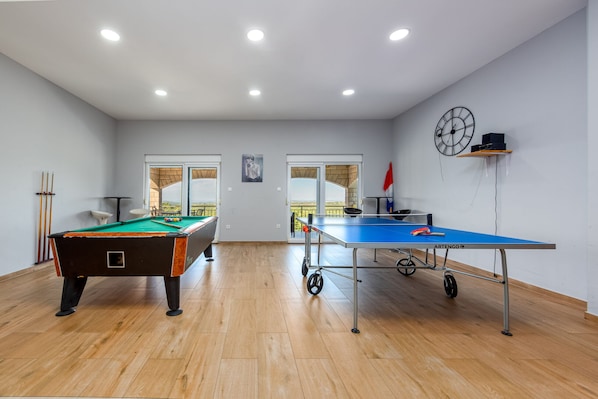 Um quarto com mesa de bilhar, mesa de pingue-pongue e equipamentos de bilhardos.