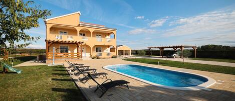 Uma casa grande com piscina, área de estar externa e um alpendre coberto.