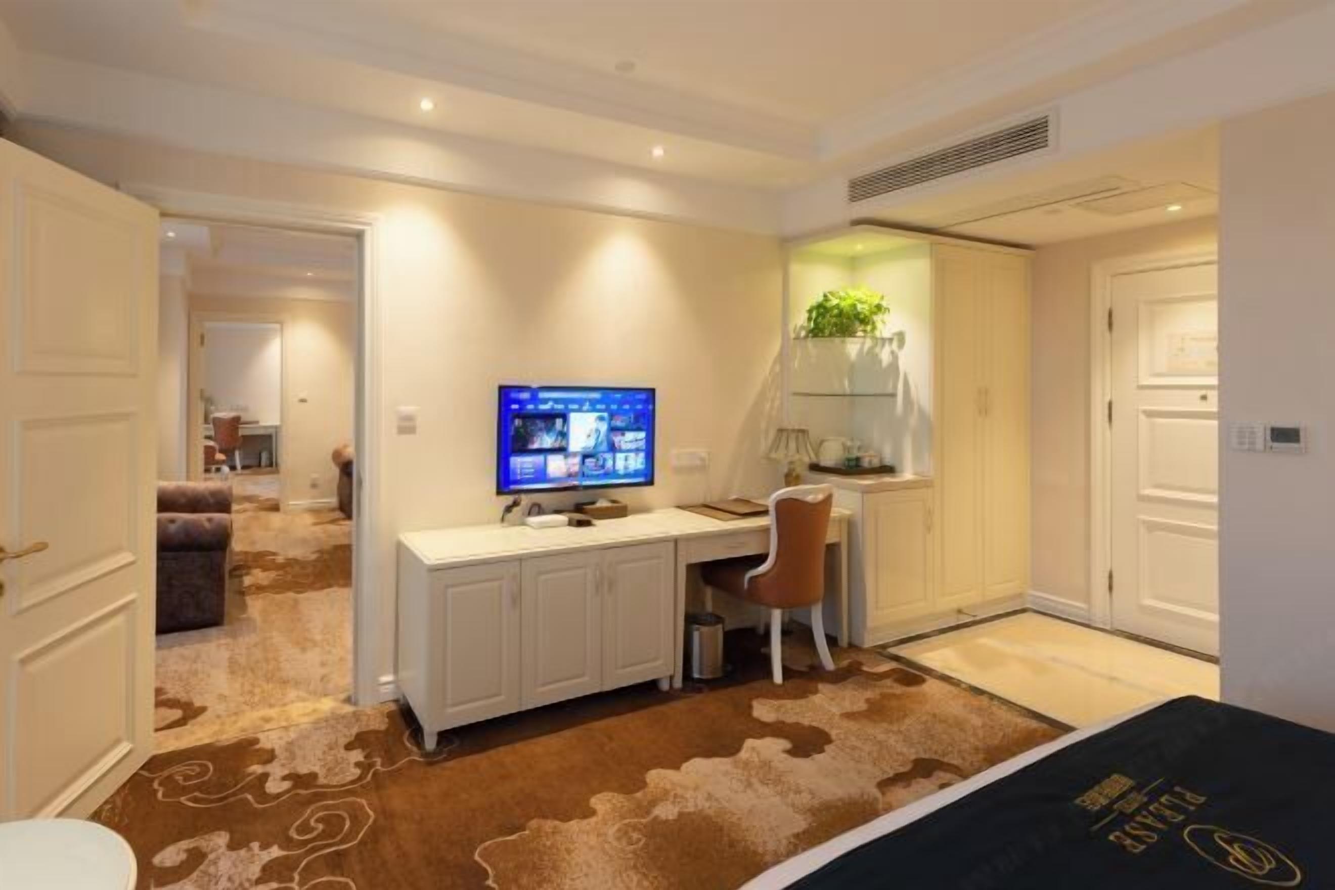 Quarto de hotel com uma escrivaninha, televisão, cadeira, cama e tapete.