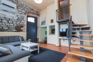 Uma sala de estar moderna com parede de pedra, um sofá modular cinza, uma mesa de centro branca e uma escada com degraus de madeira.