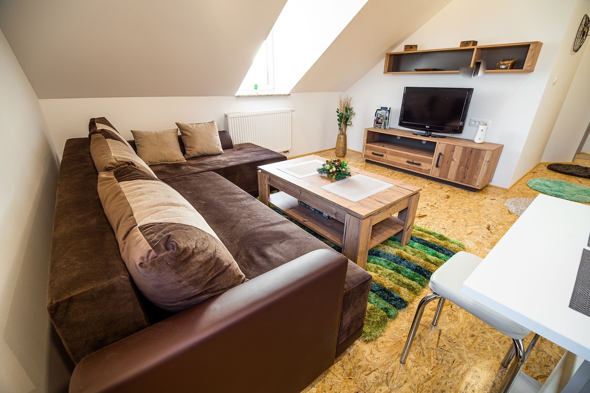 Uma sala de estar moderna com sofá em seção, mesa de centro de madeira, televisão e um pequeno espaço de jantar.