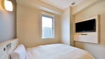 Quarto de hotel com cama, televisão presa na parede, janela e painel de controle na parede.