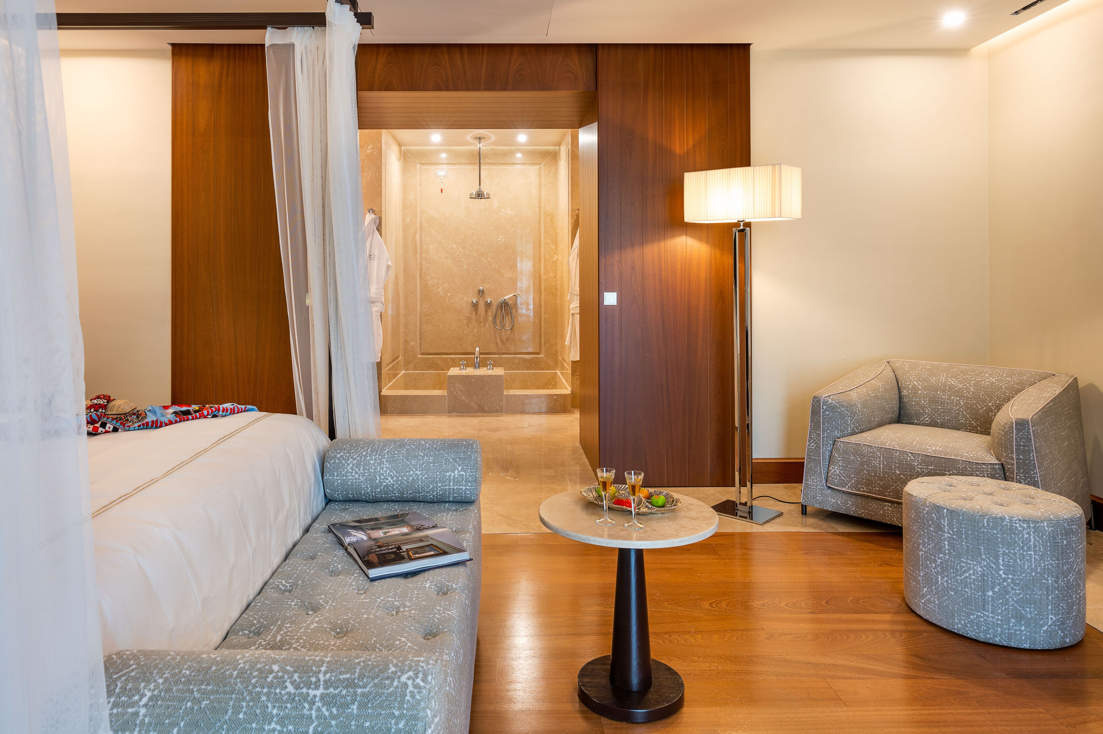 Quarto de hotel com cama, sofá, mesa redonda com abajur e área de chuveiro.
