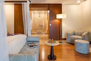Quarto de hotel com cama, sofá, mesa redonda com abajur e área de chuveiro.
