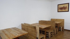 Uma sala de aula com mesas e bancos de madeira, paredes brancas e um quadro emoldurado.