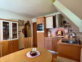 Uma cozinha compacta com armários de madeira, forno embutido, forno a lenha e área de jantar com mesa e cadeiras.