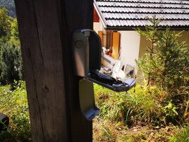 Uma porta de madeira com puxador de metal, uma janela com moldura de metal e vista para uma casa com telhado de telhas e um jardim.