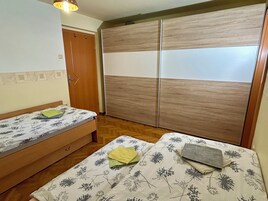 Quarto com duas camas de solteiro, um guarda-roupa de madeira e uma porta.