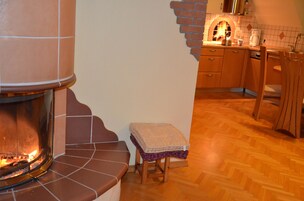 Uma cozinha com um fogão a lenha, um banquinho de madeira e painéis de azulejo.