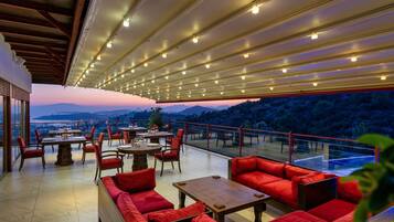 Terraço no telhado com assentos vermelhos, mesas e vista para as montanhas.