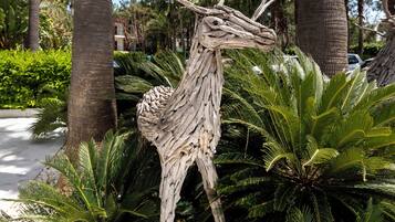 Escultura de um veado em área ajardinada com palmeiras e pedrinhas brancas.