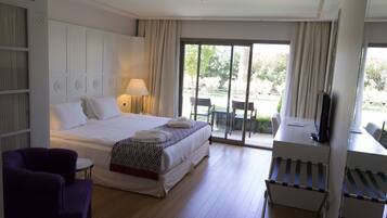 Quarto de hotel com uma cama grande, uma escrivaninha com cadeira, um poltrona roxa e uma televisão.