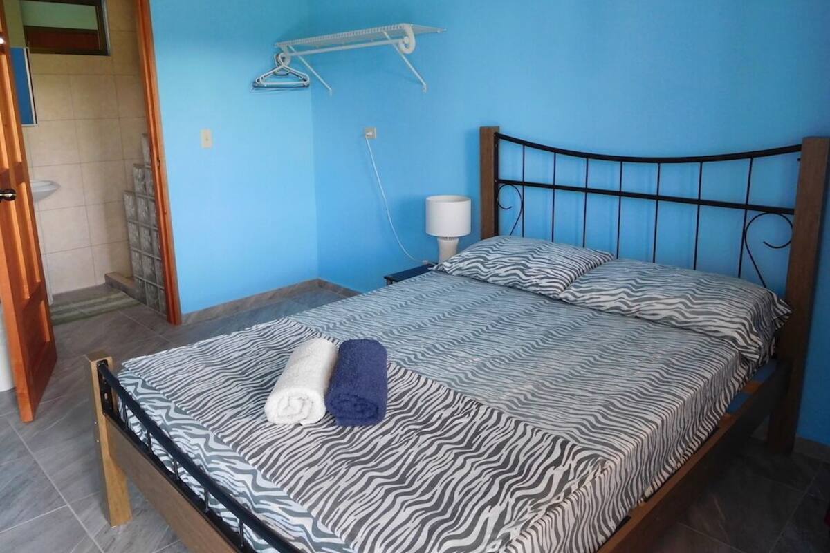 Quarto com uma cama, varal de roupa, abajur e porta para o banheiro.