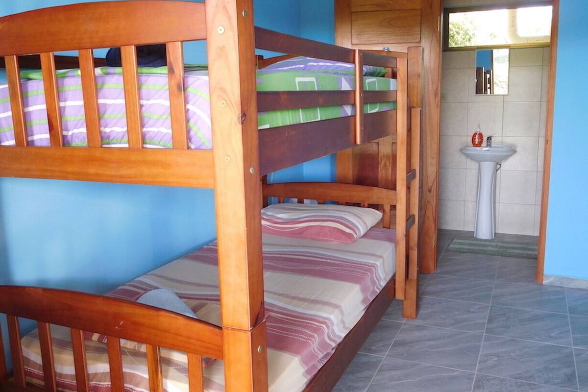 Um quarto com duas beliches de madeira, uma pia pequena e piso revestido de azulejos.