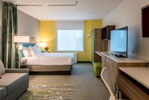 Quarto de hotel com cama, secretária, televisão, cadeira e janela.