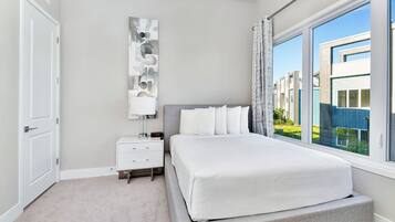 Quarto com cama grande, mesa de cabeceira, luminária na parede e janela com vista para edifícios.