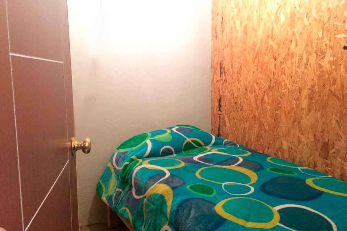 Quarto pequeno com cama, parede de madeira e porta.
