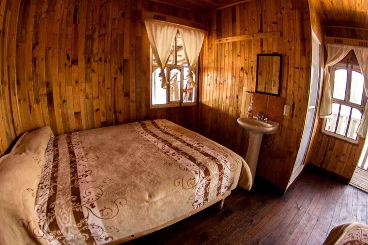 Quarto de madeira com cama, pia e janela com cortinas.