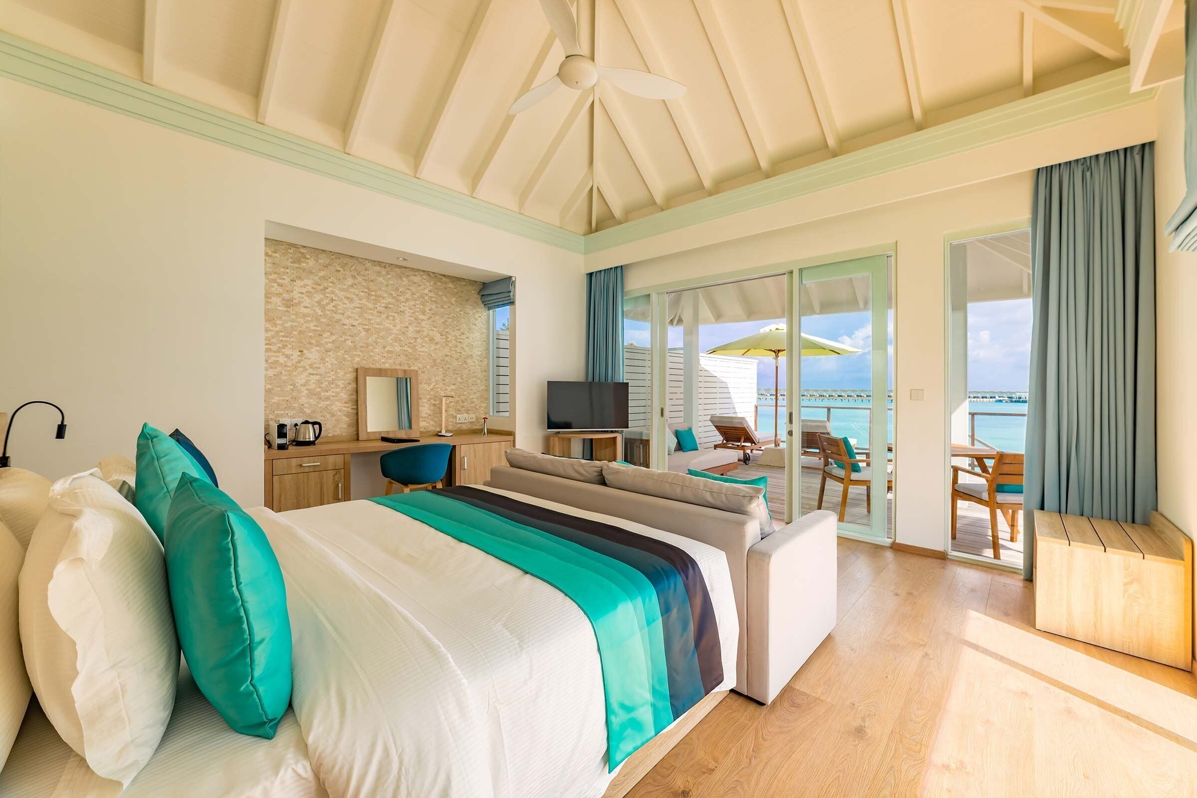 Um quarto espaçoso com uma cama grande, uma escrivaninha, uma televisão e uma varanda com vista para o mar.