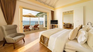 Quarto de hotel com uma cama grande, uma cadeira, uma TV e vista para o mar através da porta de vidro.