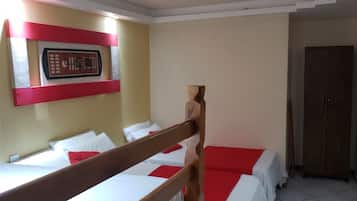 Quarto de hotel com cabeceira de madeira, duas camas de solteiro com roupa de cama vermelha e branca, um relógio de parede e uma porta de madeira.