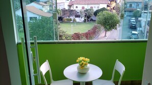 Um quarto com parede verde, uma mesa branca com um vaso de flores amarelas e duas cadeiras brancas.