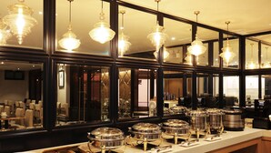 Disposição de buffet com diversas estações de serviço, um espelho grande refletindo o espaço e lustres elegantes.
