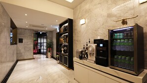 Um hall de hotel moderno com piso de mármore, um balcão de recepção, uma máquina de vendas automática e uma escultura decorativa.