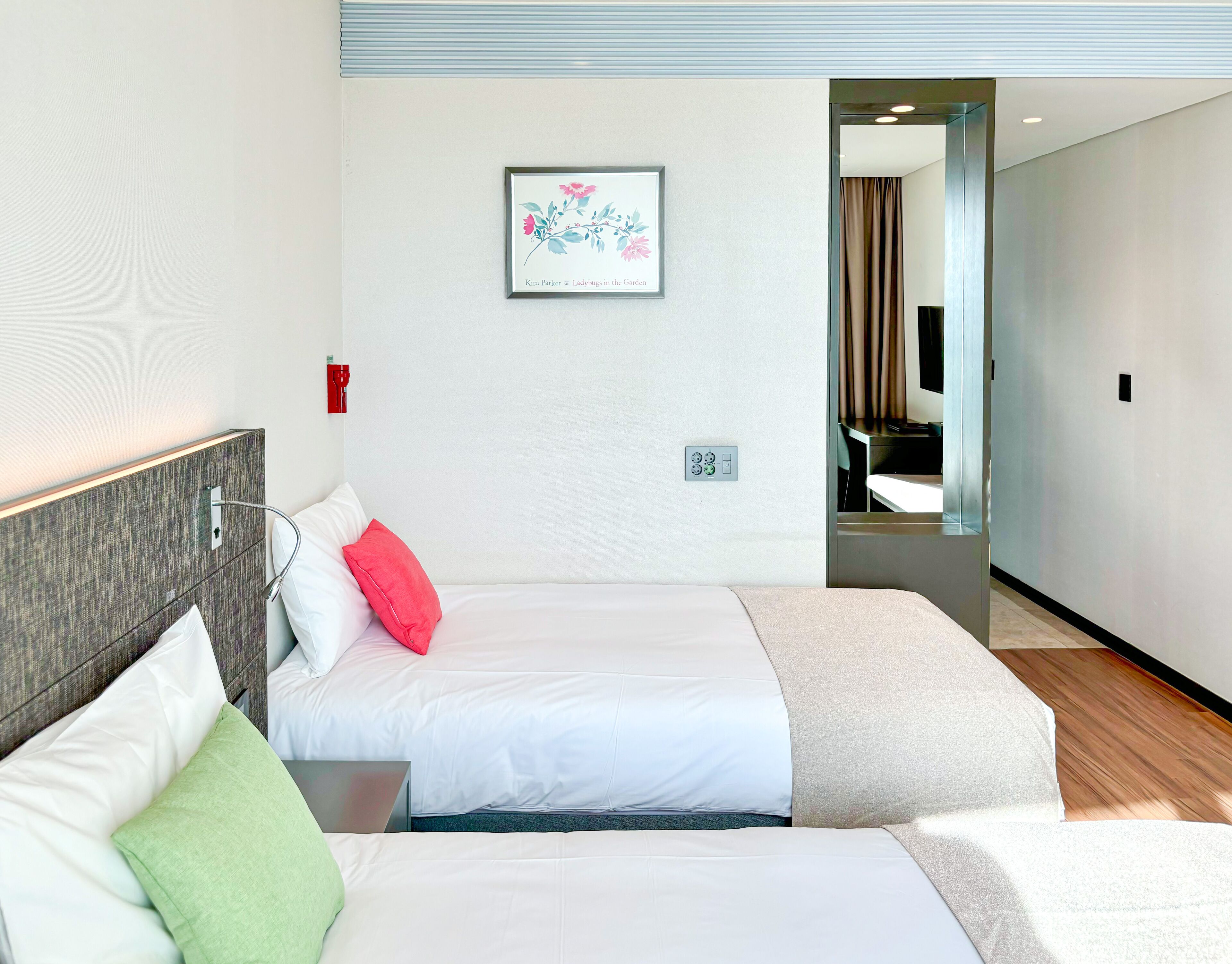 Quarto de hotel com duas camas, uma obra de arte emoldurada na parede e um espelho refletindo parte do espaço.