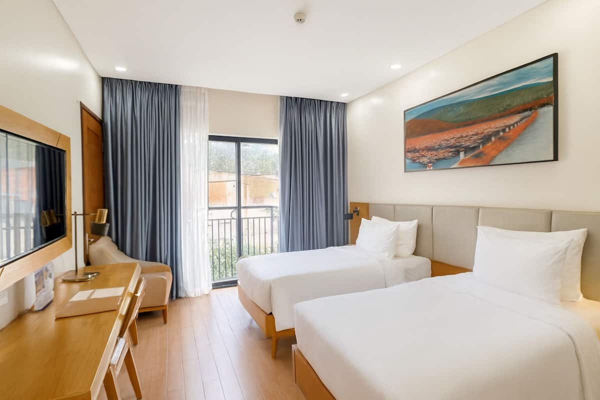 Quarto de hotel com duas camas, uma mesa, uma televisão e uma varanda com cortinas.