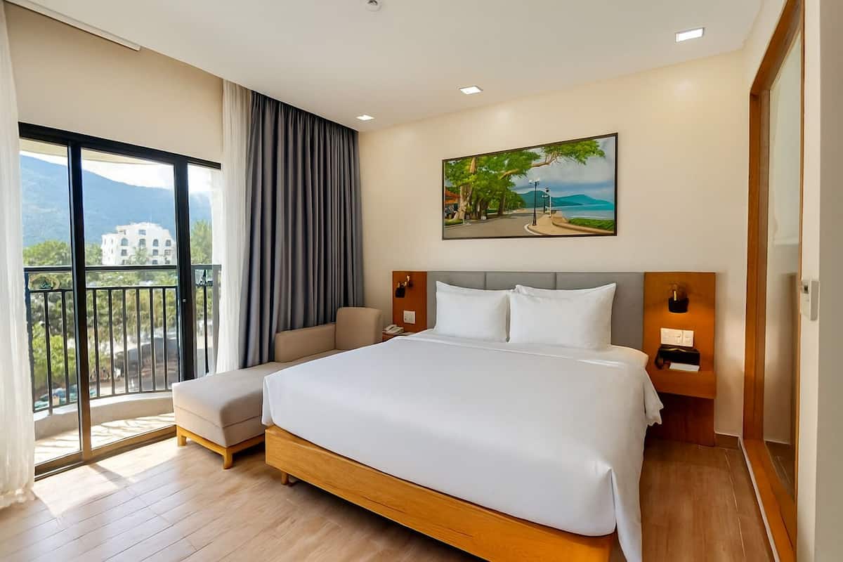 Quarto de hotel moderno com uma cama grande, mesa de cabeceira, uma cadeira, um quadro na parede e uma varanda com vista.