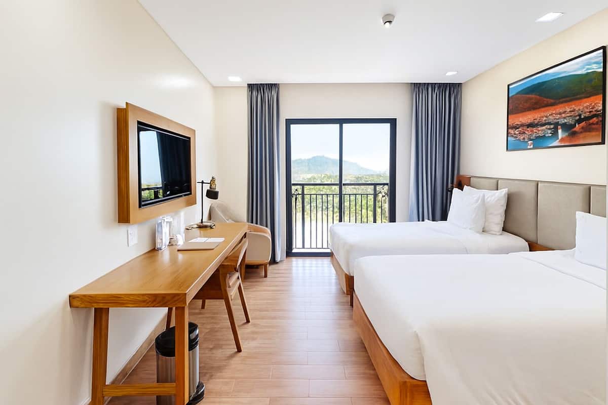 Quarto de hotel com escrivaninha, duas camas, televisão e varanda com vista panorâmica.