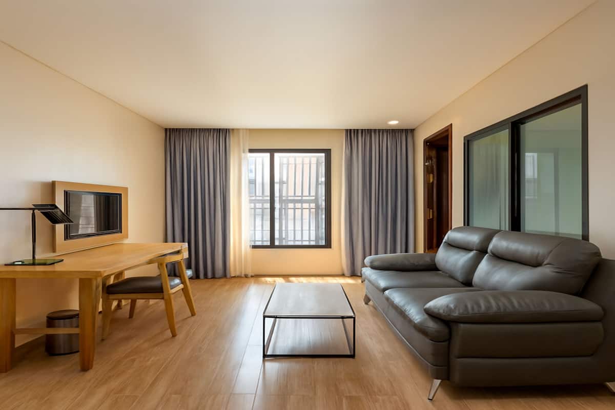 Uma sala de estar moderna com uma escrivaninha de madeira, um sofá de couro, uma televisão e uma janela grande com cortinas.