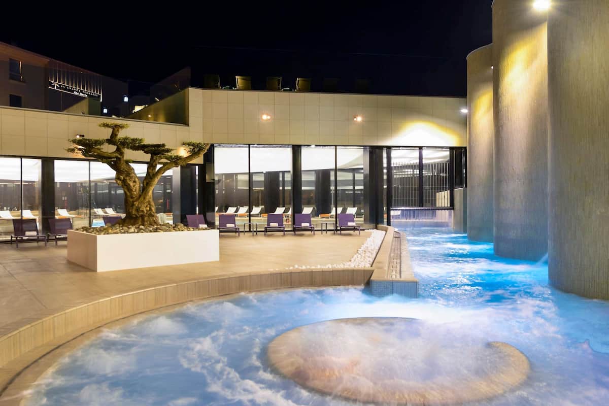 Área de spa com hidromassagem, espreguiçadeiras e uma grande árvore.