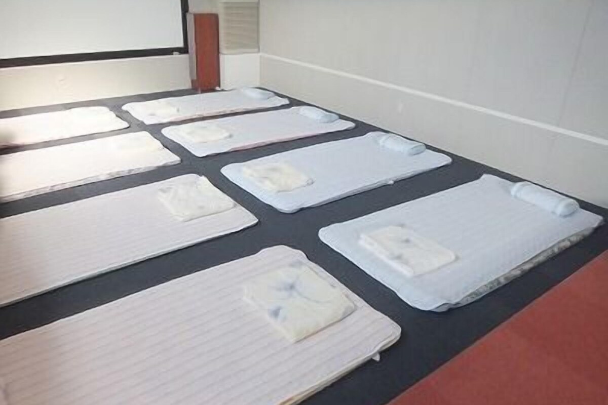 Um quarto com várias camas dispostas em fileiras, cada uma com travesseiro e cobertor.