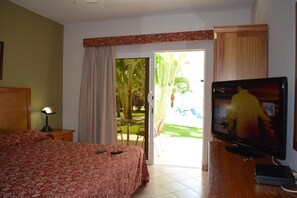Quarto de hotel com cama, televisão, mesa de cabeceira e vista para a área externa.