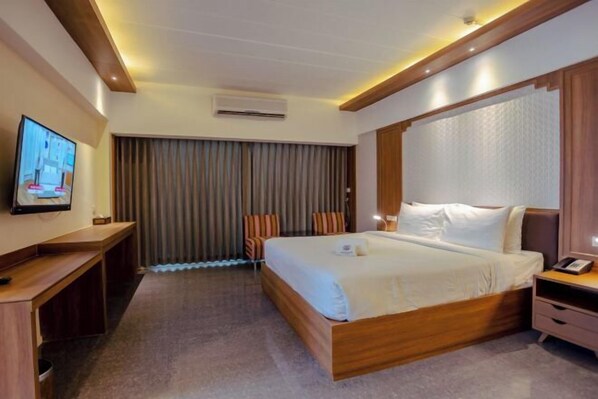 Quarto de hotel com uma cama grande, uma escrivaninha, uma televisão e uma janela com cortinas.