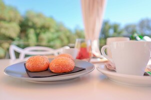 Uma mesa com um prato de dois pãezinhos, uma xícara e um copo de suco.