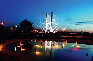 Uma ponte com uma torre central e cabos, cercada por um corpo d'água que reflete luzes.