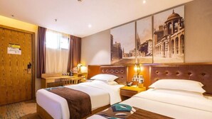 Quarto de hotel com duas camas, uma escrivaninha, uma cadeira, mesa de cabeceira e uma janela grande com cortinas.