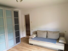Quarto com sofá, porta de correr de vidro e piso de madeira.