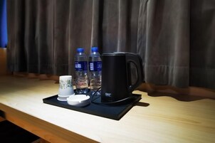 Uma bandeja com uma cafeteira preta, duas garrafas de água, uma caneca branca e uma xícara pequena branca sobre uma mesa de madeira.
