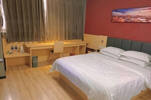 Quarto de hotel com cama, escrivaninha, cadeira, lixeira e um quadro na parede.