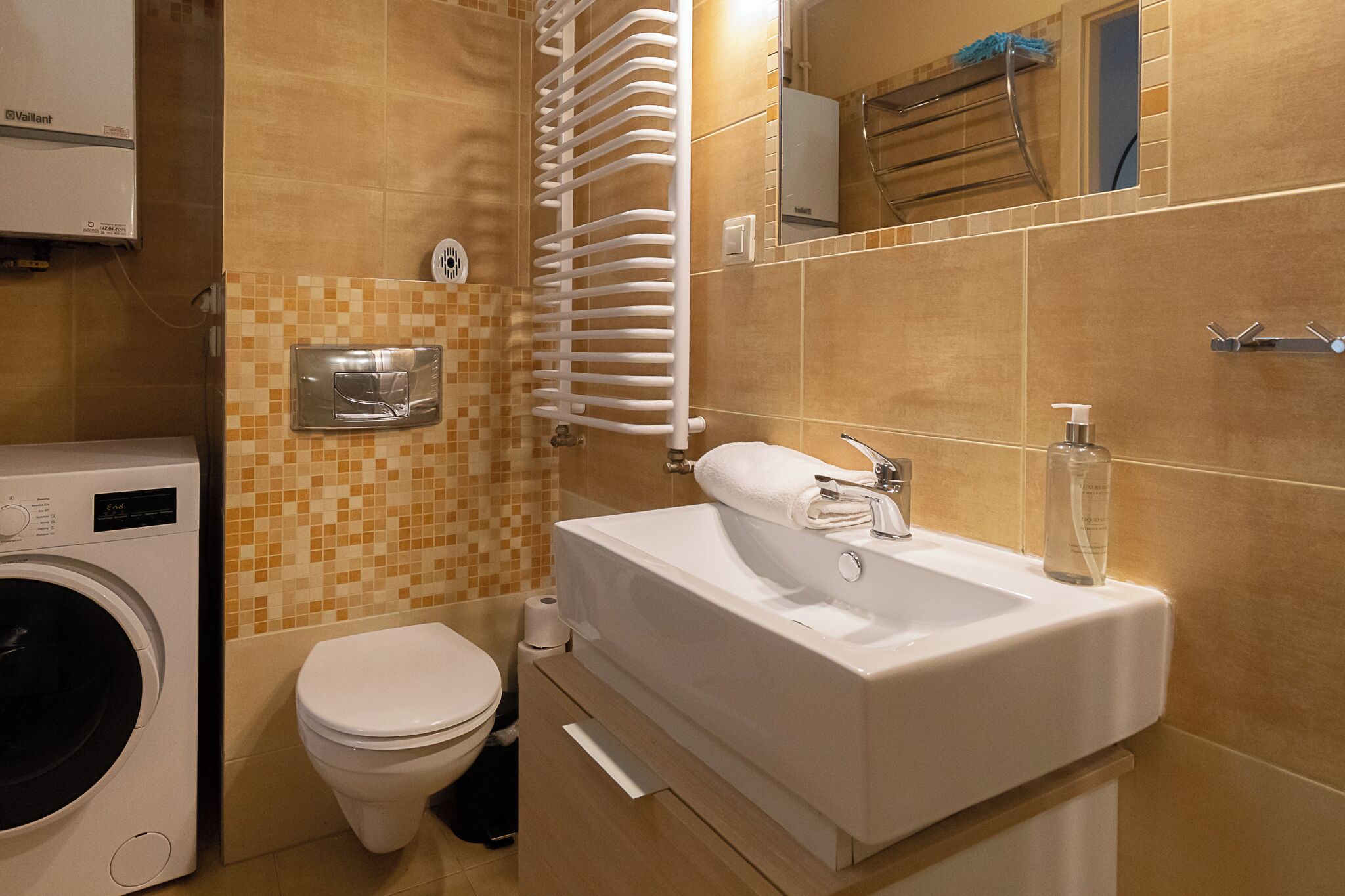 Casa de banho com máquina de lavar, sanita, lavatório e suporte para toalhas.