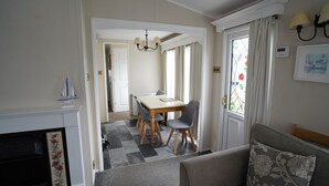 Um quarto com lareira, uma mesa de jantar com cadeiras, um sofá e uma janela com cortinas.