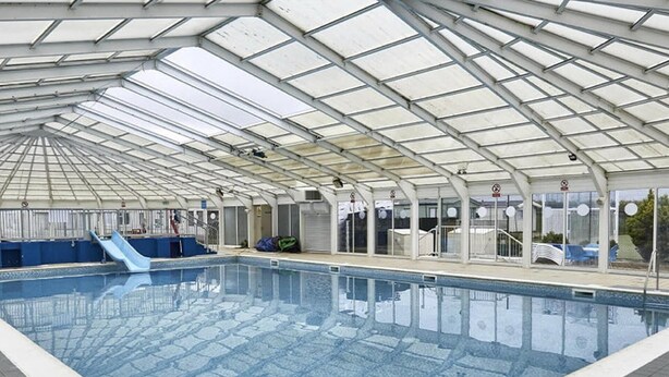 Piscina interna com teto de vidro, escorregador e piso azulejado.