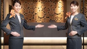 Duas pessoas vestidas formalmente, com crachás, em um saguão com parede de madeira e balcão de recepção.