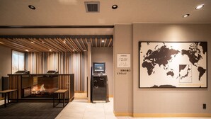 Um lobby com balcão de recepção de madeira, lareira, mapa-múndi na parede e quiosque de autoatendimento.