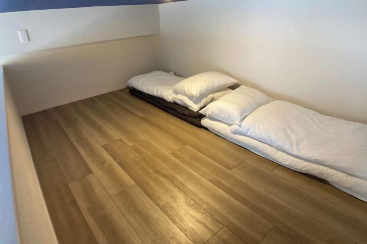 Um quarto pequeno e estreito, com soalho de madeira e uma cama simples com roupa de cama branca.